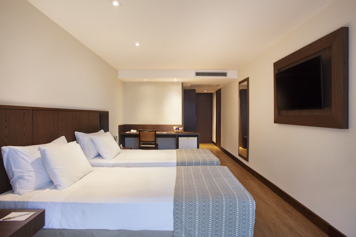 Quarto de hotel com duas camas, uma escrivaninha e um espelho.
