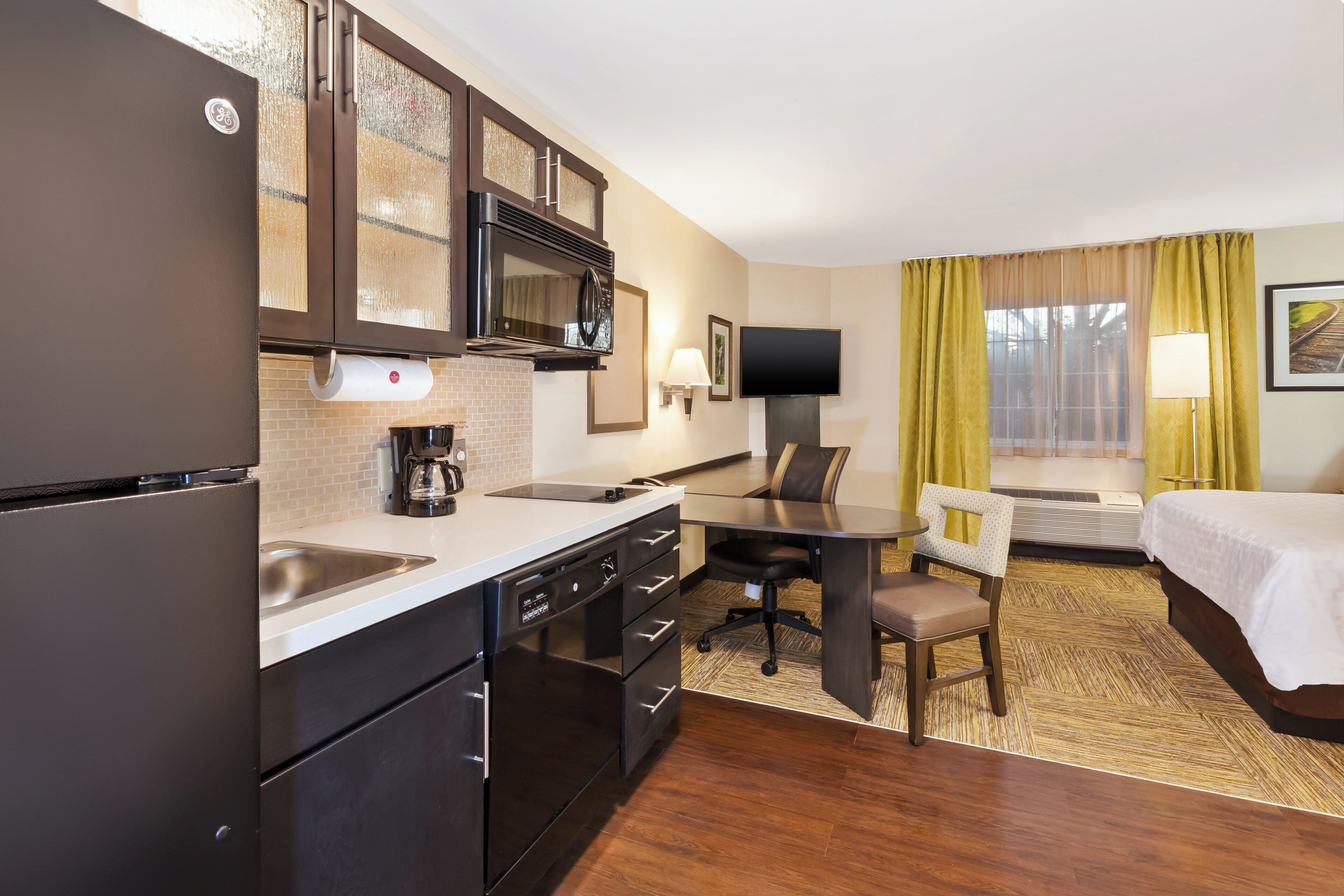 Quarto de hotel com cozinha compacta, uma cama, escrivaninha e televisão.