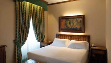 Quarto de hotel com cama, mesa de cabeceira, quadro na parede e janela com cortinas.