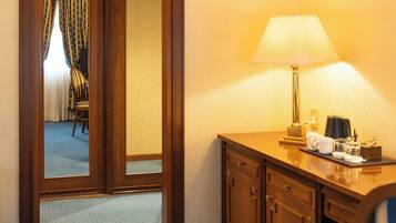 Quarto de hotel com uma secretária de madeira, candeeiro, cadeira, espelho e porta que dá para outro espaço.