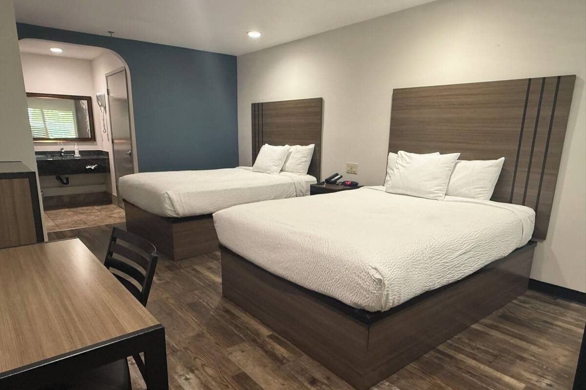 Quarto de hotel com duas camas, uma escrivaninha e banheiro com espelho.