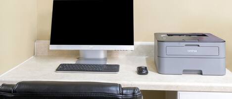 Uma mesa com monitor de computador, teclado, rato e impressora Brother.