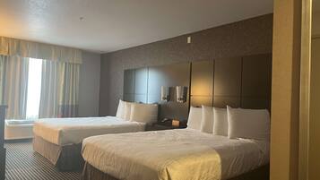 Quarto de hotel com duas camas, uma cabeceira grande, luminárias de cabeceira e um relógio na mesa de apoio.