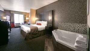 Quarto de hotel com uma cama grande, área de estar com uma poltrona e uma escrivaninha, banheira espaçosa e janela com cortinas.