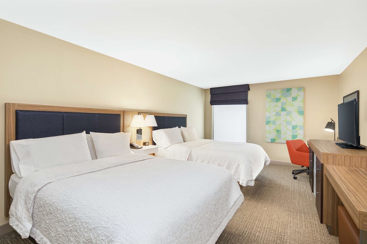 Quarto de hotel com duas camas, uma mesa com televisão e uma cadeira.