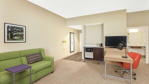 Uma sala de estar moderna com um sofá verde, uma mesinha, uma televisão e uma escrivaninha com uma cadeira laranja.