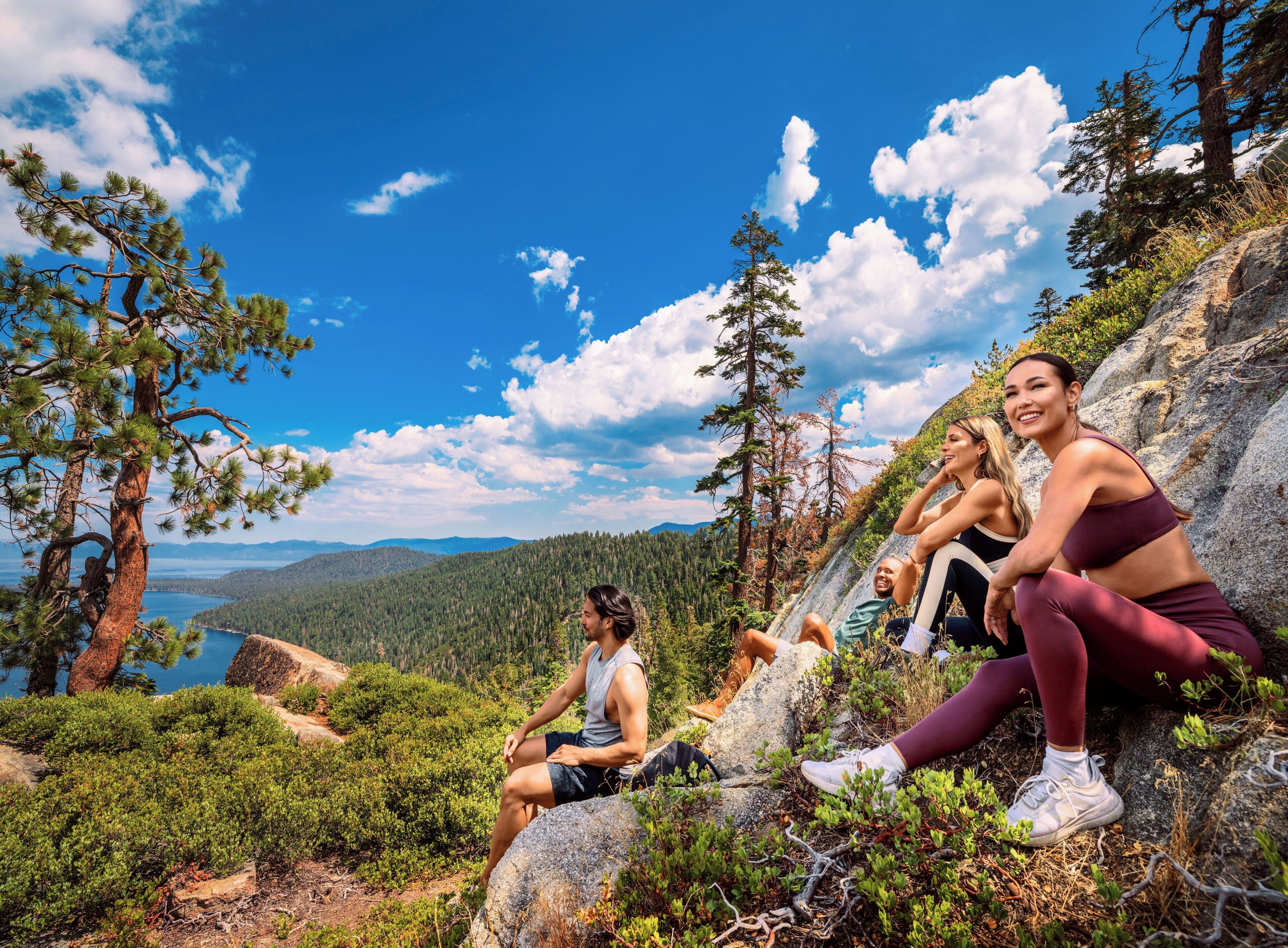 Um grupo de pessoas sentadas em pedras, com uma paisagem montanhosa e um lago ao fundo.