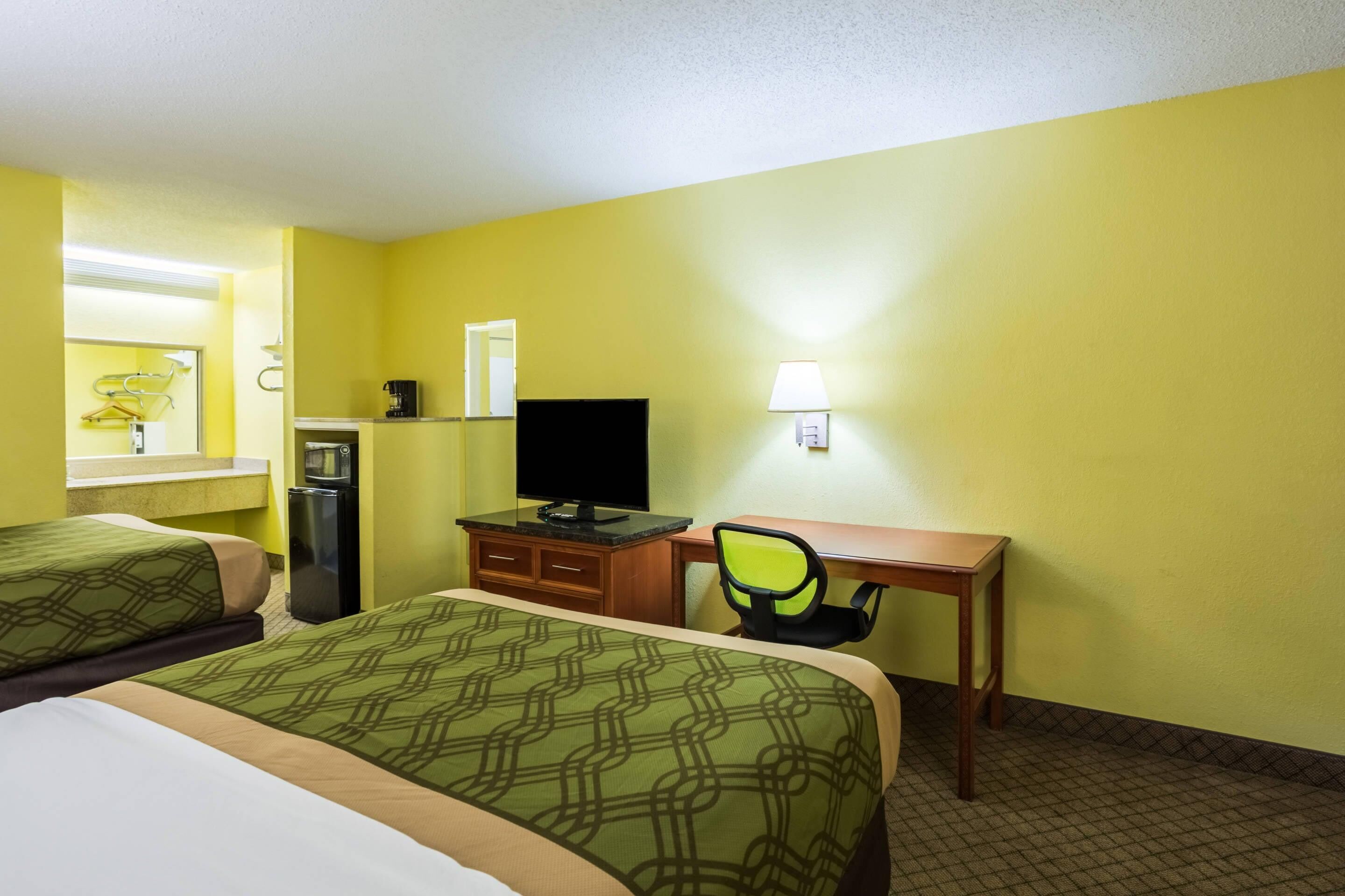 Quarto de hotel com duas camas, uma escrivaninha, televisão, abajur e espelho.