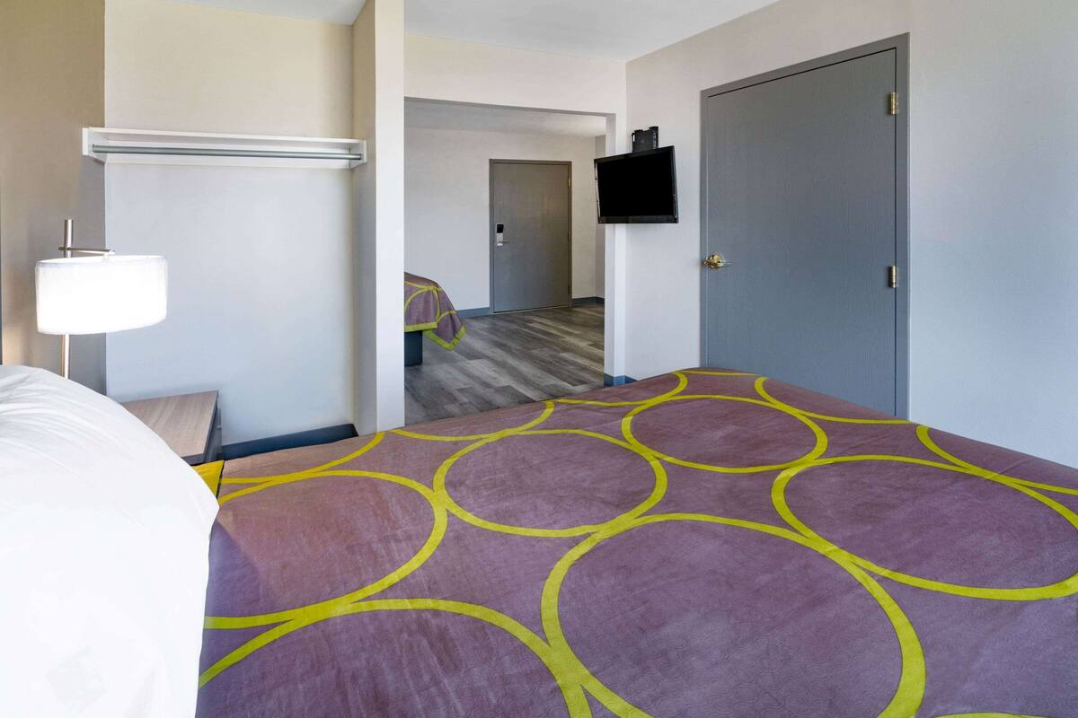 Quarto de hotel com uma cama, uma televisão de tela plana fixada na parede e uma porta que dá para outro quarto.