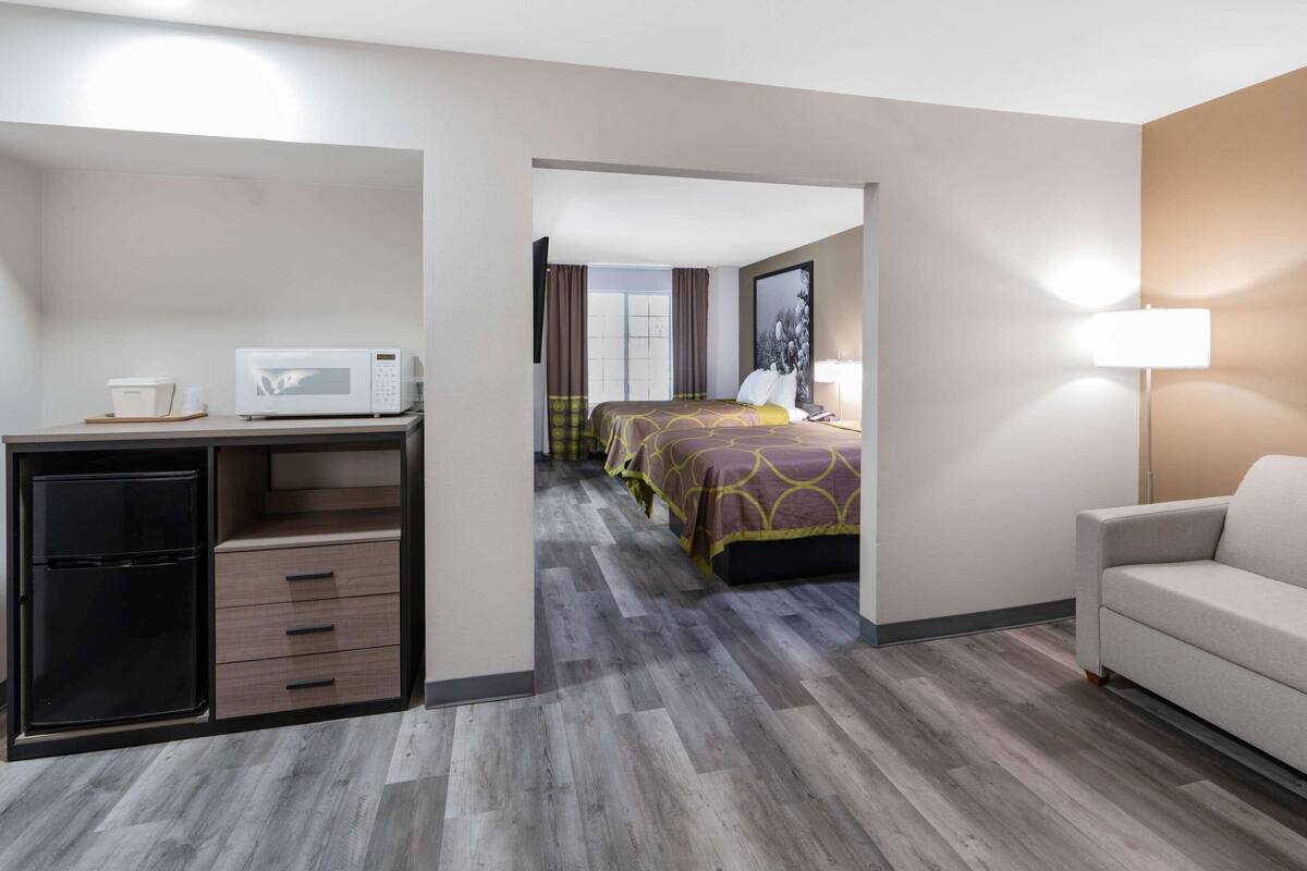 Quarto de hotel com uma cama, uma escrivaninha com micro-ondas, uma cadeira e um abajur.