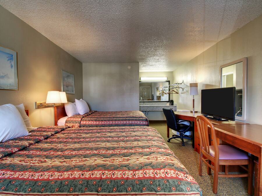 Quarto de hotel com duas camas, uma mesa com cadeira, televisão e espelho.