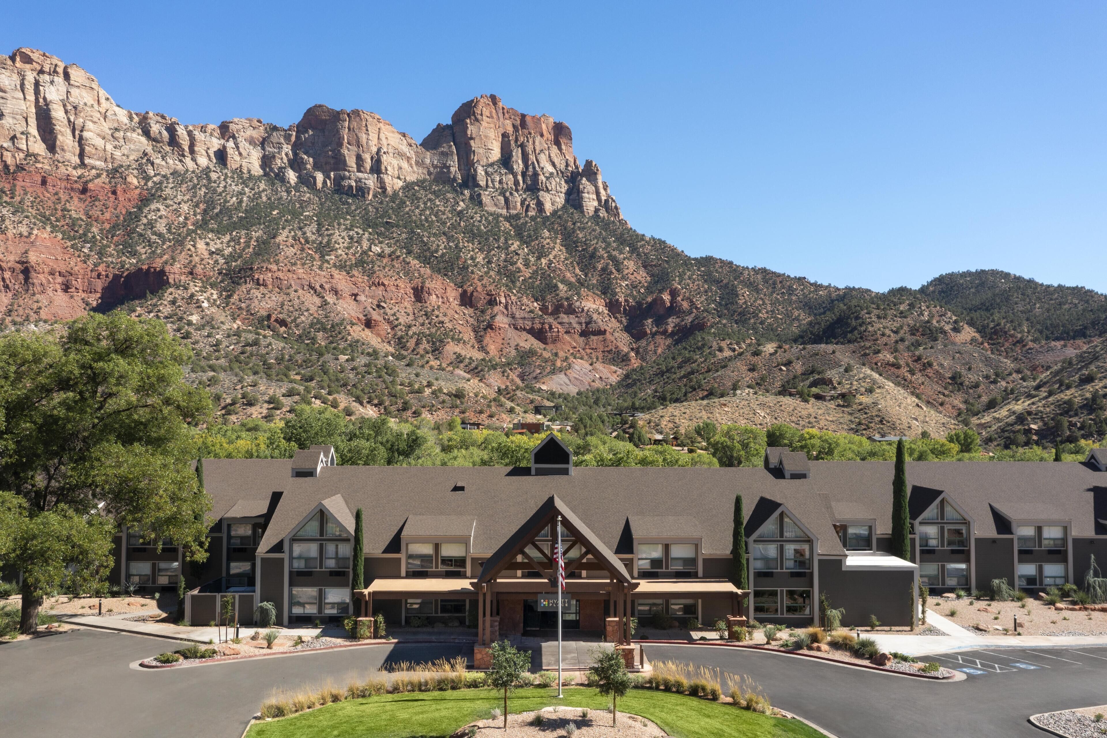 Um hotel com design arquitetónico moderno, apresentando uma entrada imponente com telhado triangular, grandes janelas e um parque de estacionamento à frente.