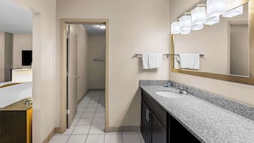 Uma casa de banho moderna com bancada de granito, um espelho grande e zona de duche visível através de uma porta aberta.