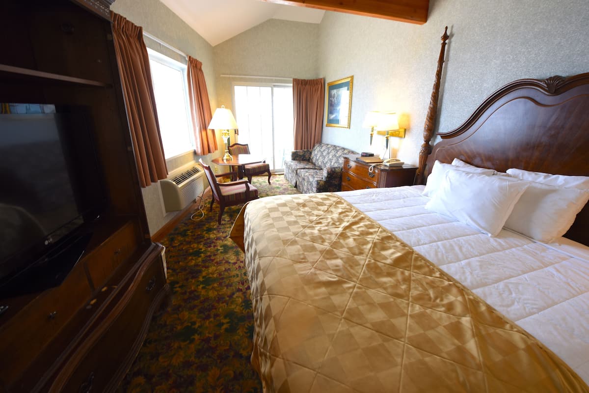 Quarto de hotel com uma cama grande, televisão, escrivaninha com cadeira e sofá.