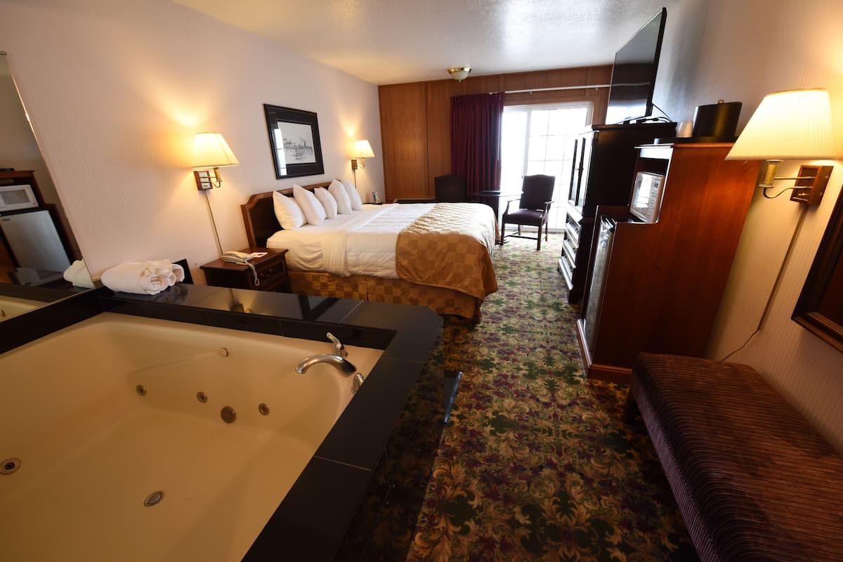 Quarto de hotel com uma cama grande, um sofá separado, uma escrivaninha com cadeira, televisão e banheiro com banheira e pia.