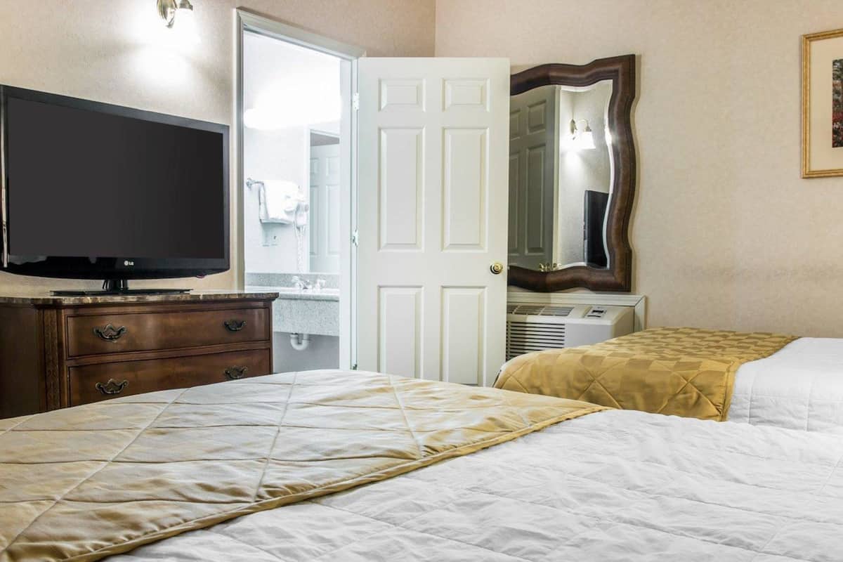 Quarto de hotel com uma cama, televisão, penteadeira, espelho e porta para o banheiro.