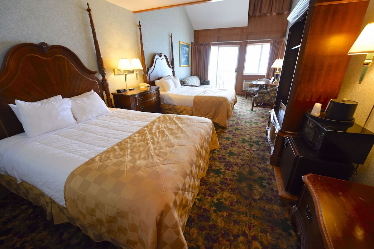 Quarto de hotel com duas camas, uma escrivaninha, uma cadeira, televisão e janela.