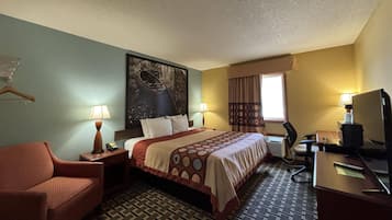 Quarto de hotel com uma cama, duas luminárias de cabeceira, uma mesa com computador, uma cadeira e uma televisão.