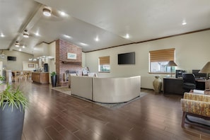 Um hall amplo com área de estar em curva, lareira de tijolos e cozinha moderna ao fundo.