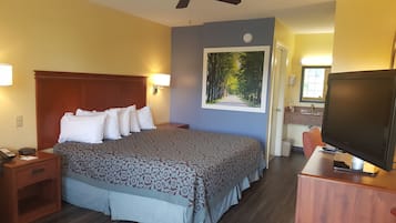 Quarto de hotel com cama grande, televisão, escrivaninha e banheiro visível através de uma porta aberta.