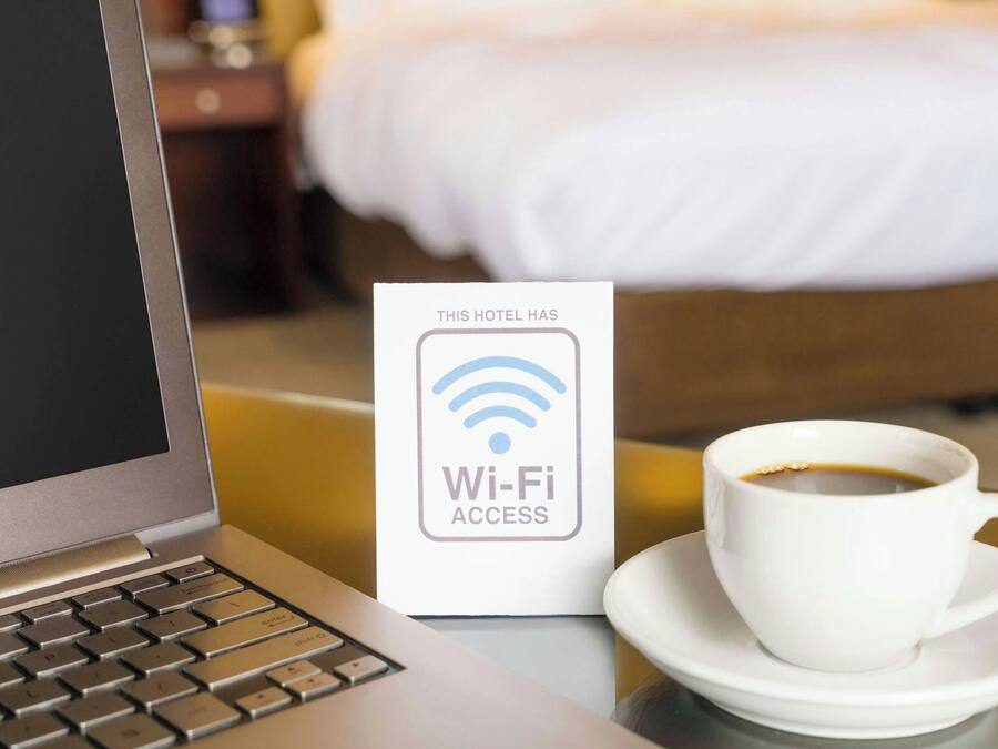 Um laptop, um sinal de acesso Wi-Fi e uma xícara de café sobre uma mesa.