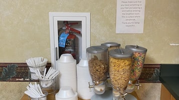 Estação de café da manhã com copos de papel, guardanapos e distribuidores de cereal.