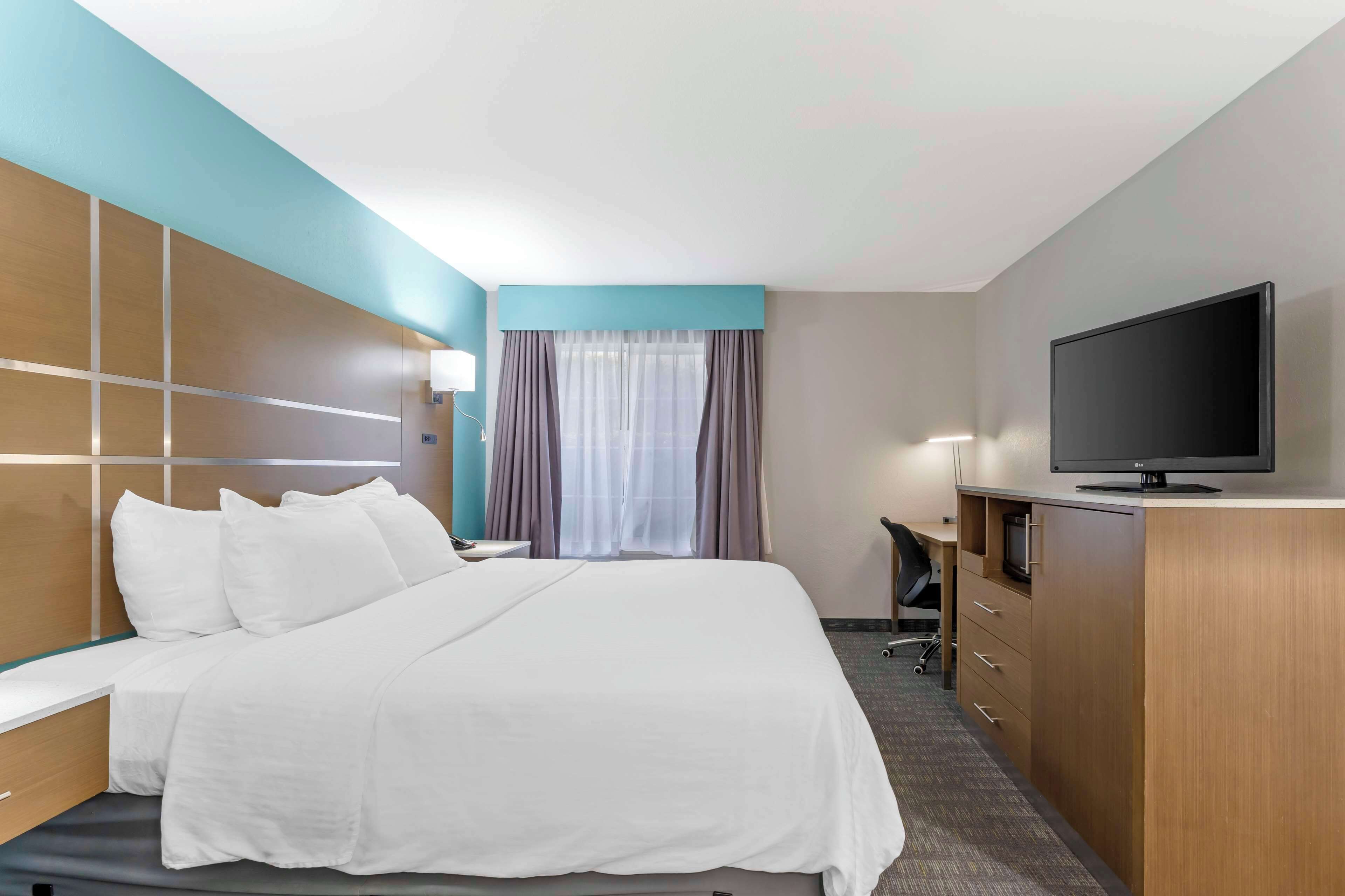 Quarto de hotel com uma cama grande, televisão, escrivaninha e janela com cortinas.