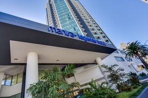 Um hotel moderno com um destaque para a placa 'Manila Legends Hotel', apresentando uma estrutura de vários andares com varandas e vegetação exuberante em ambientes internos.