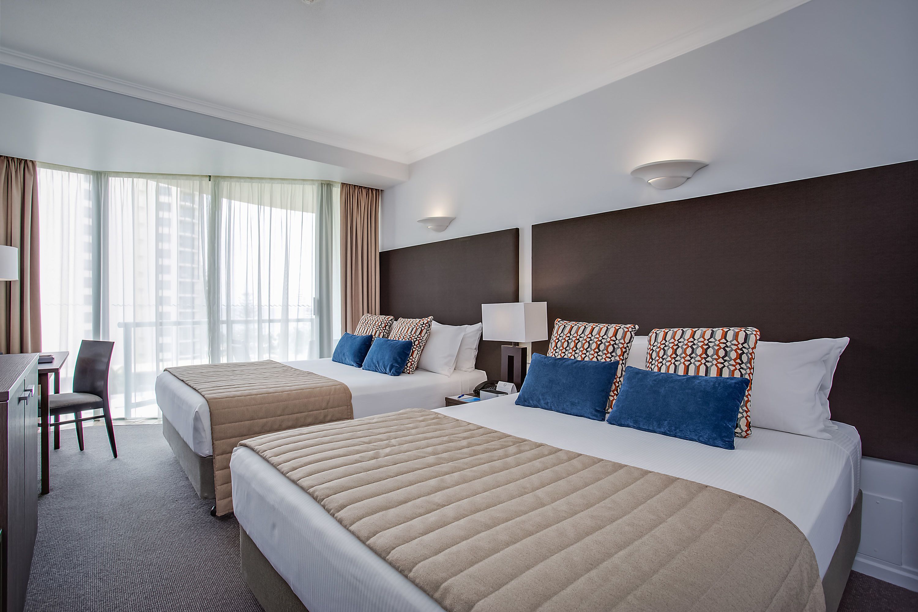 Quarto de hotel com duas camas, uma escrivaninha e uma cadeira.