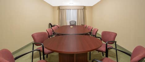 Uma sala de conferências com uma mesa redonda, cadeiras estofadas em vermelho e piso coberto de carpete.