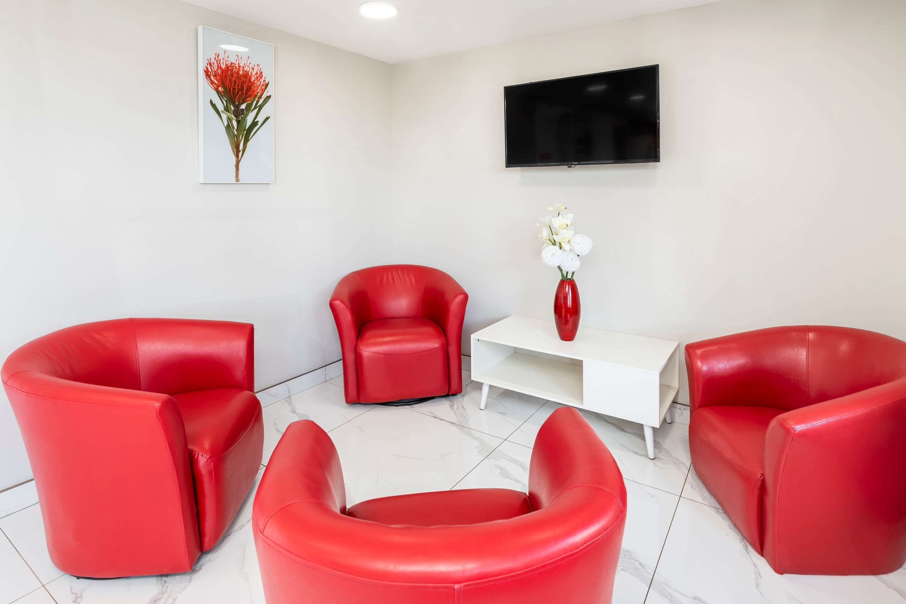 Uma sala de estar moderna com três sofás de couro vermelho, uma mesa de centro branca e uma TV de tela plana na parede.