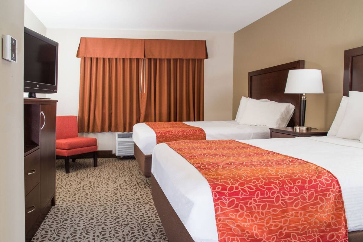 Quarto de hotel com duas camas, televisão, escrivaninha, cadeira e janela com cortinas.