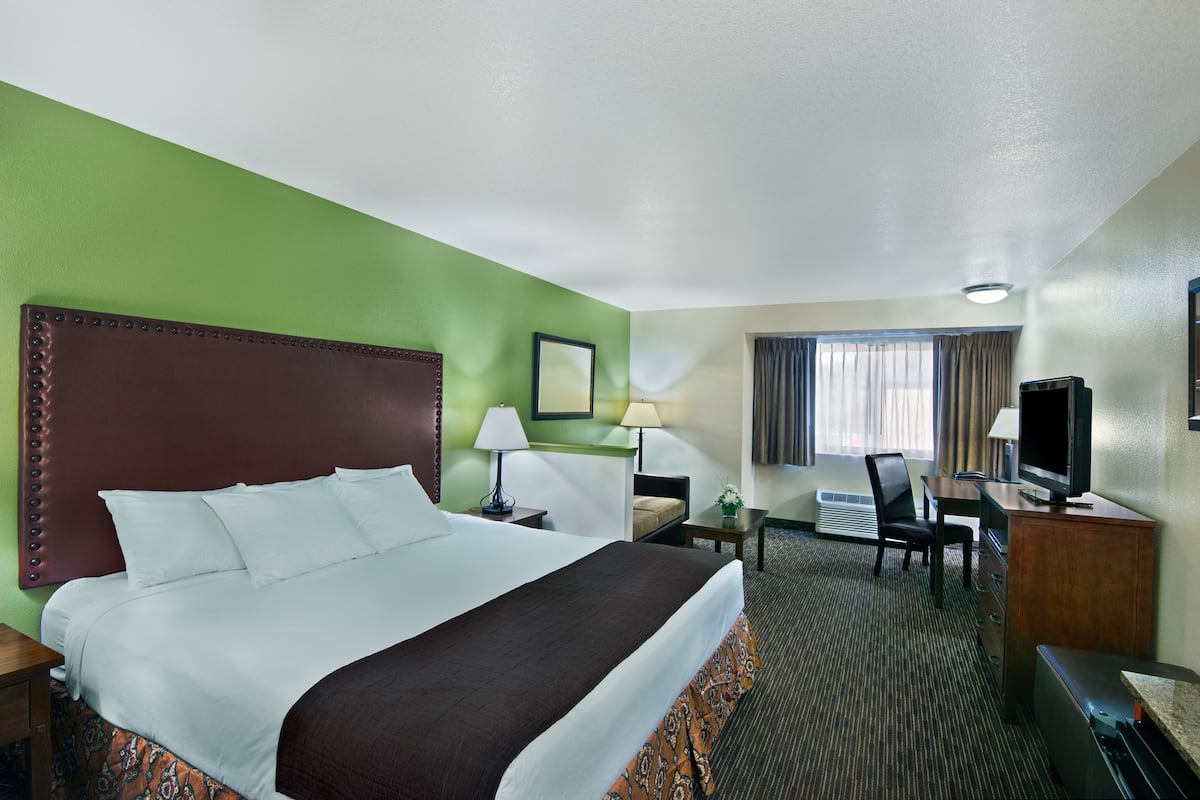 Quarto de hotel com uma cama grande, uma escrivaninha com cadeira, televisão e janela com cortinas.