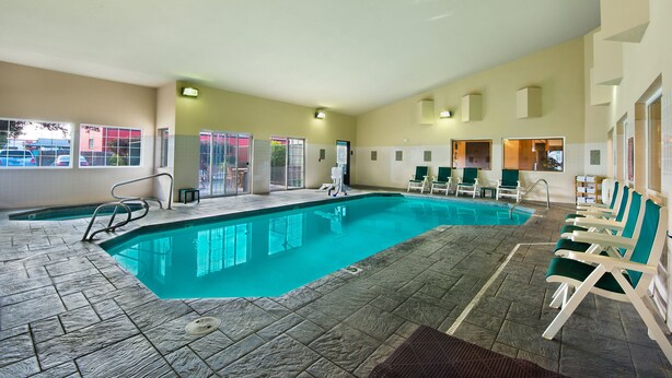Piscina interior com piso de pedra, escada para piscina e várias cadeiras de descanso.