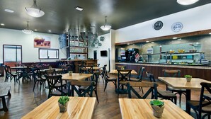 Interior de restaurante com mesas e cadeiras de madeira e luminárias pendentes.