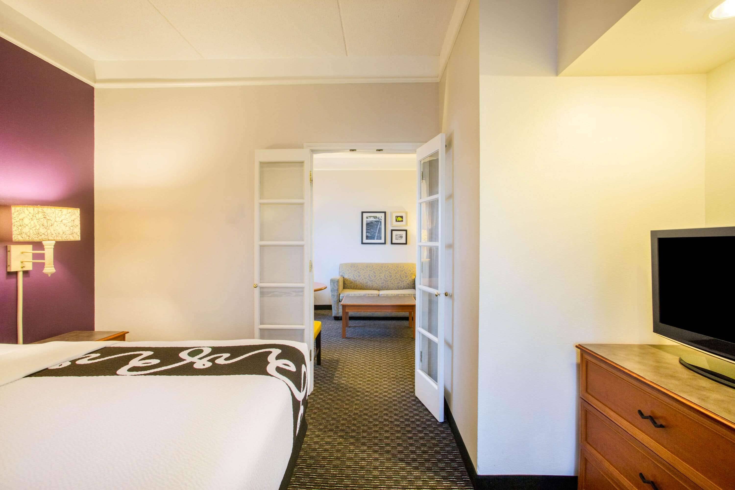 Quarto de hotel com cama, televisão, escrivaninha e cadeira.