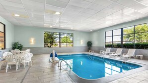 Piscina interior com água azul cristalina, rodeada por espreguiçadeiras brancas e uma área de refeições com cadeiras brancas.