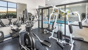 Academia com aparelhos de cardio, equipamentos de musculação e vista para uma piscina.
