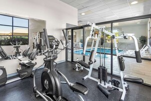 Academia com aparelhos de cardio, equipamentos de musculação e vista para uma piscina.