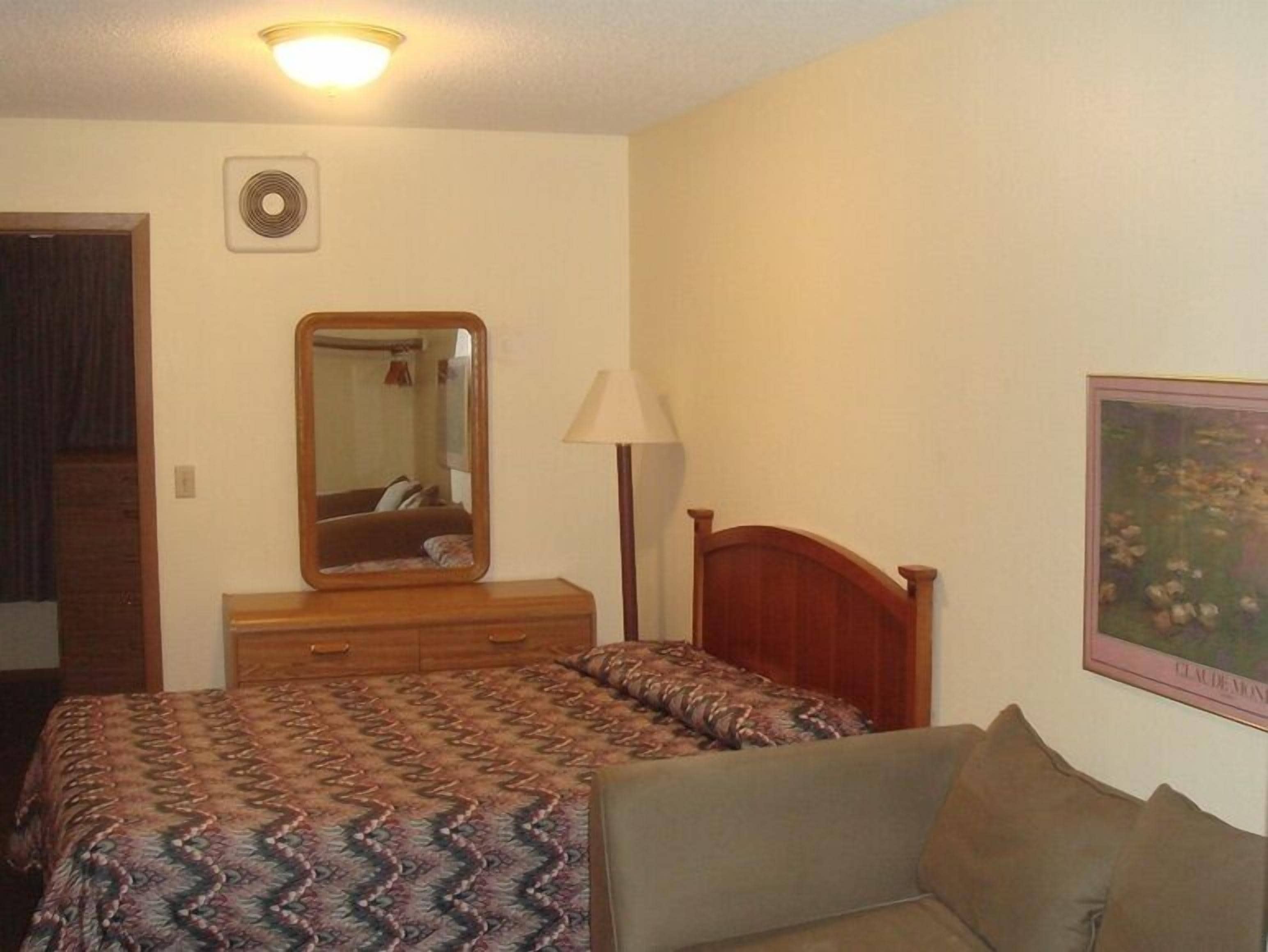 Um quarto com cama, penteadeira, mesa de cabeceira, luminária, espelho e um quadro na parede.