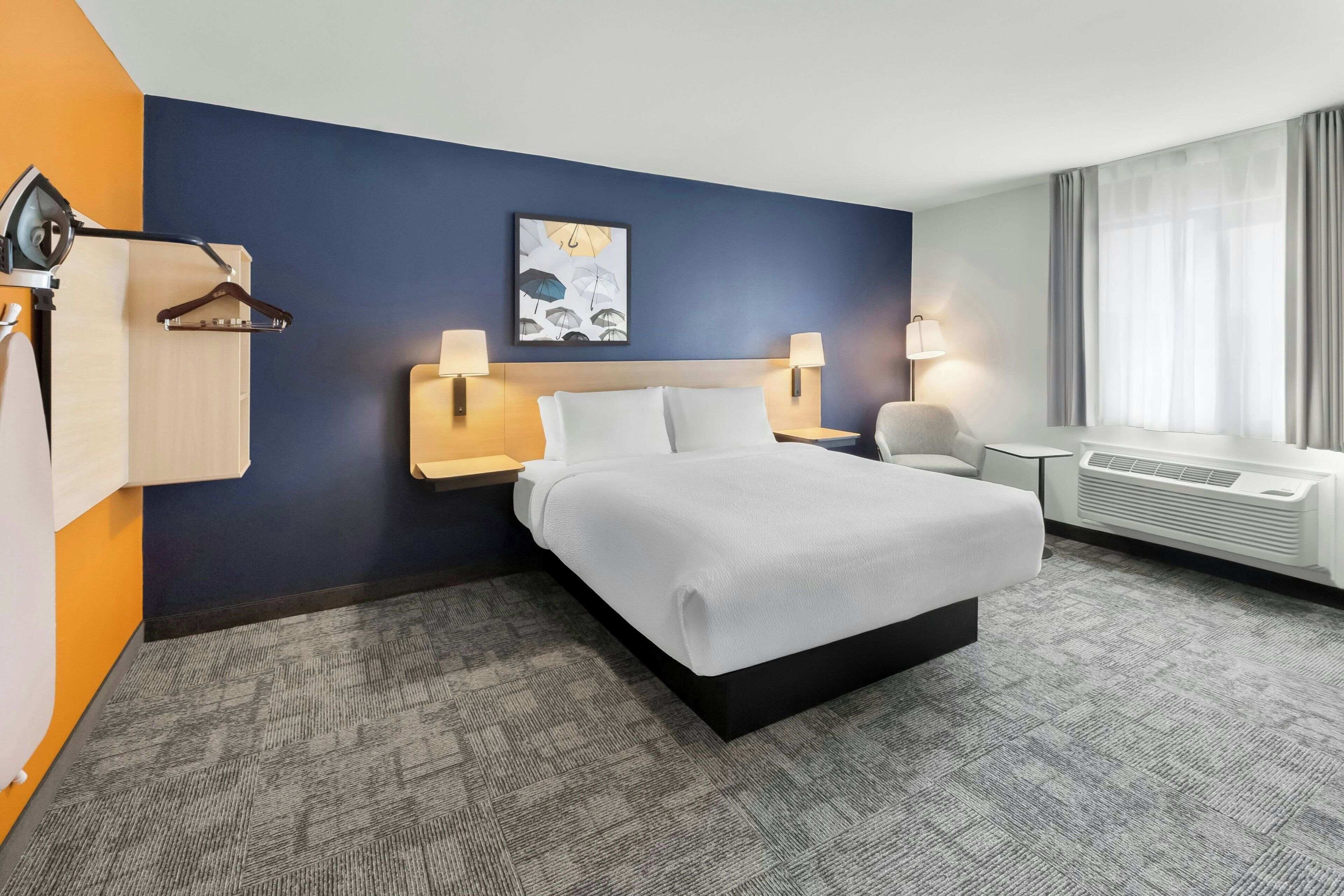 Quarto de hotel com cama, mesas de cabeceira, luminárias, um quadro na parede e uma janela com cortinas.