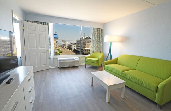 Uma sala de estar moderna com um sofá verde, uma mesa de centro branca e uma janela iluminada com vista para edifícios.