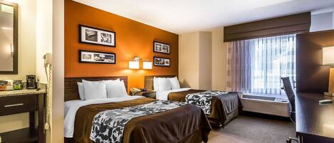 Quarto de hotel com duas camas, uma escrivaninha com cafeteira, um espelho e quadros nas paredes.
