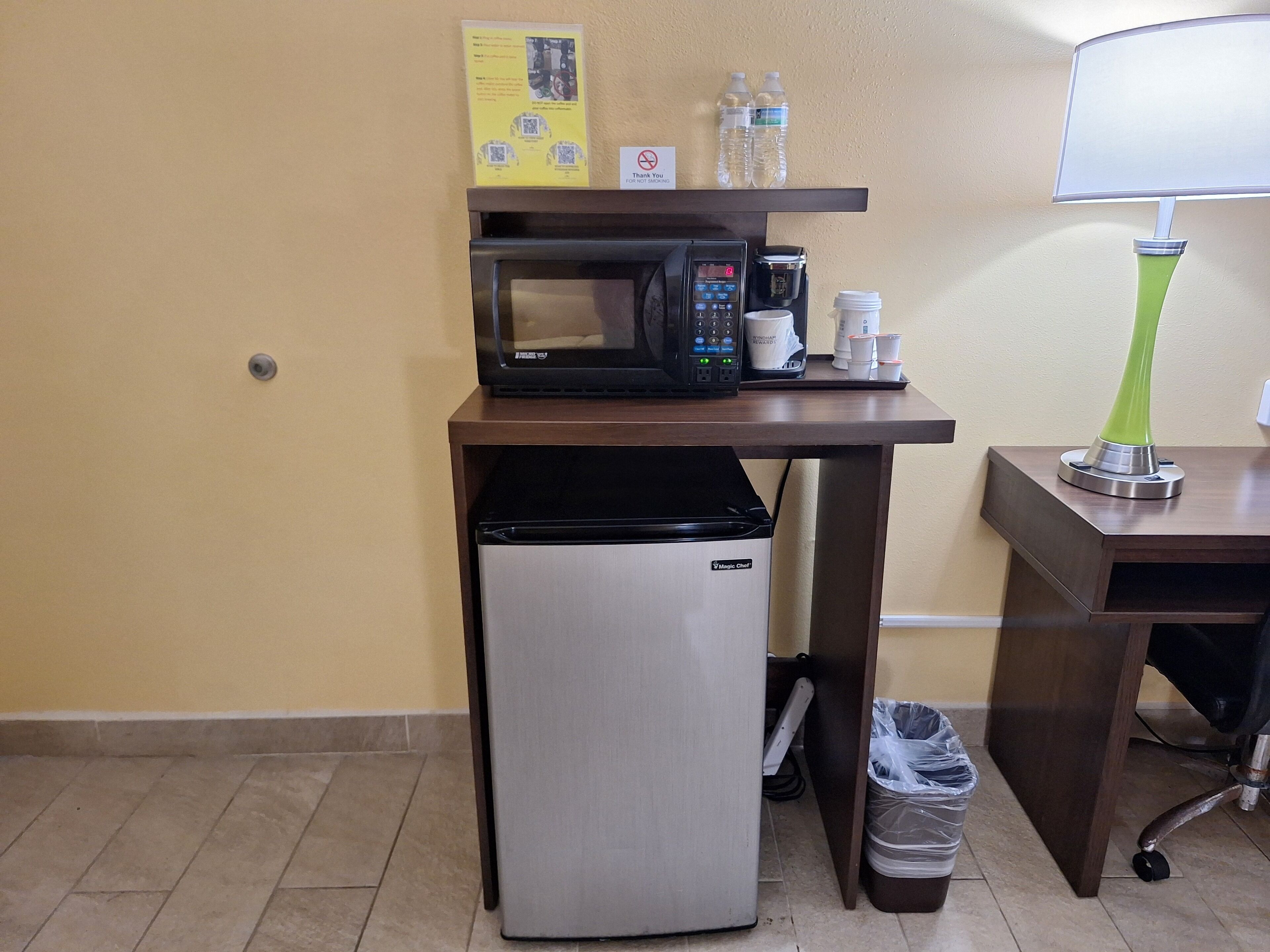 Uma cozinha compacta com micro-ondas, cafeteira e garrafas de água em uma prateleira.