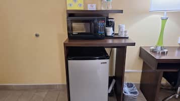 Uma cozinha compacta com micro-ondas, cafeteira e garrafas de água em uma prateleira.