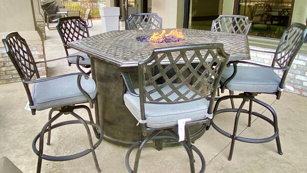 Pátio externo com mesa redonda de metal e seis cadeiras com assentos acolchoados.