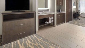 Quarto de hotel moderno com televisão de tela plana, penteadeira com espelho, cafeteira e escrivaninha com cadeira.