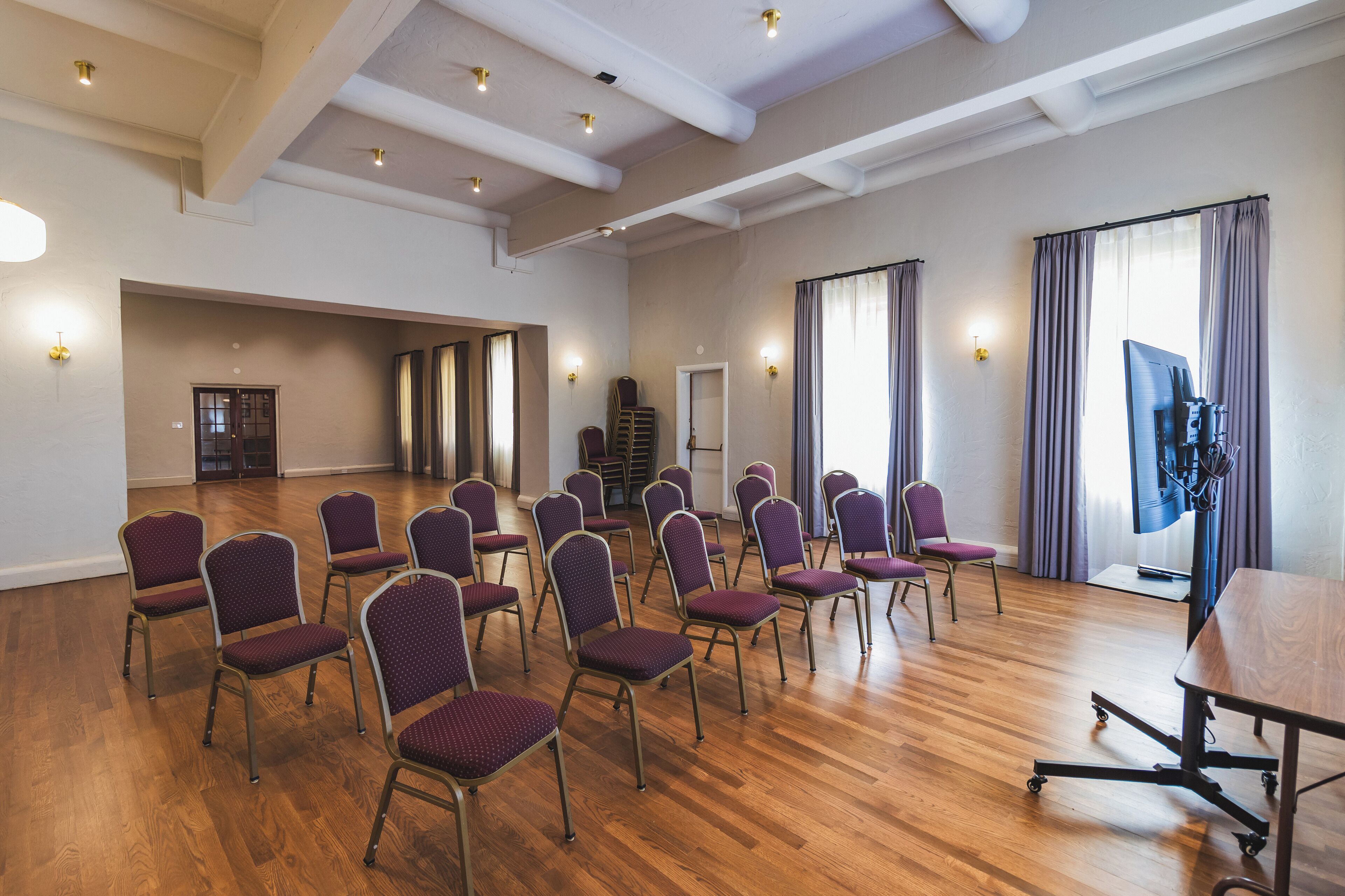Uma sala de conferência com fileiras de cadeiras roxas, uma mesa grande e uma televisão.