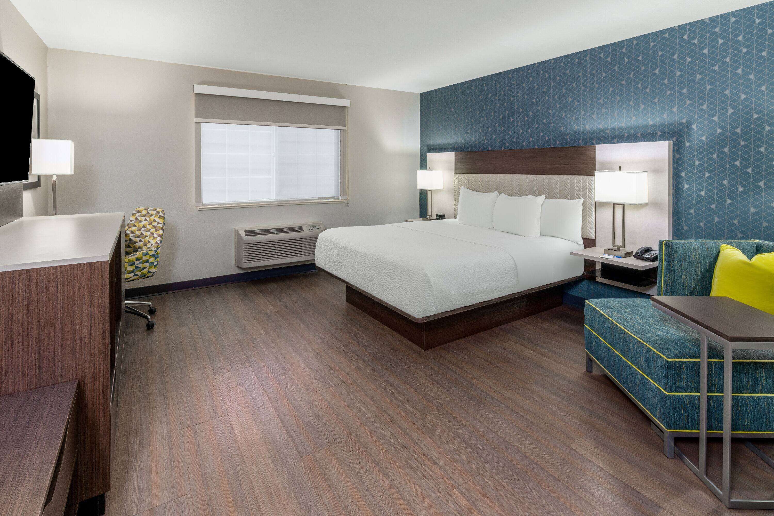 Quarto de hotel com cama grande, mesas de cabeceira, escrivaninha, cadeira e sofá.