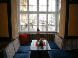 Quarto com uma grande janela, um sofá azul, uma pequena mesa com um vaso de flores e almofadas com padrão listrado.